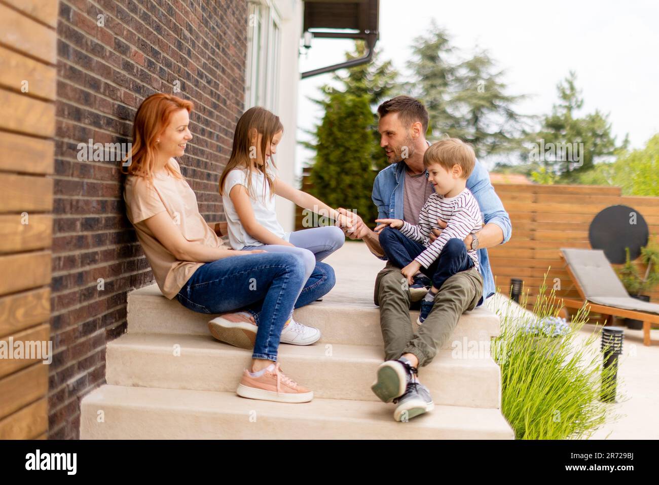 Family with a mother, father, son and daughter sitting outside on steps ...