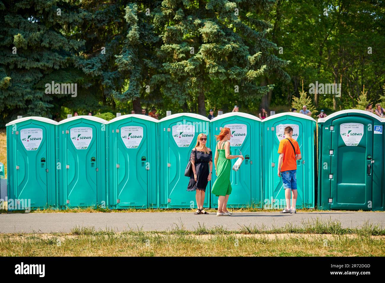 A group of people standing in front of a row of plastic toilet cabins ...