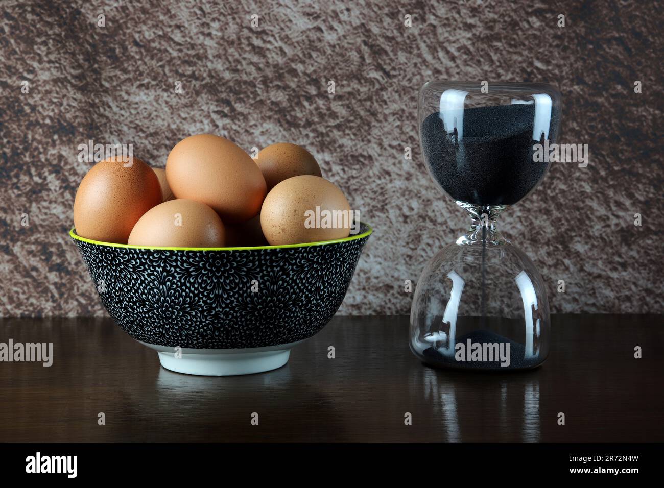 Sand glass egg timer with bowl of fresh eggs on a varnished wooden ...