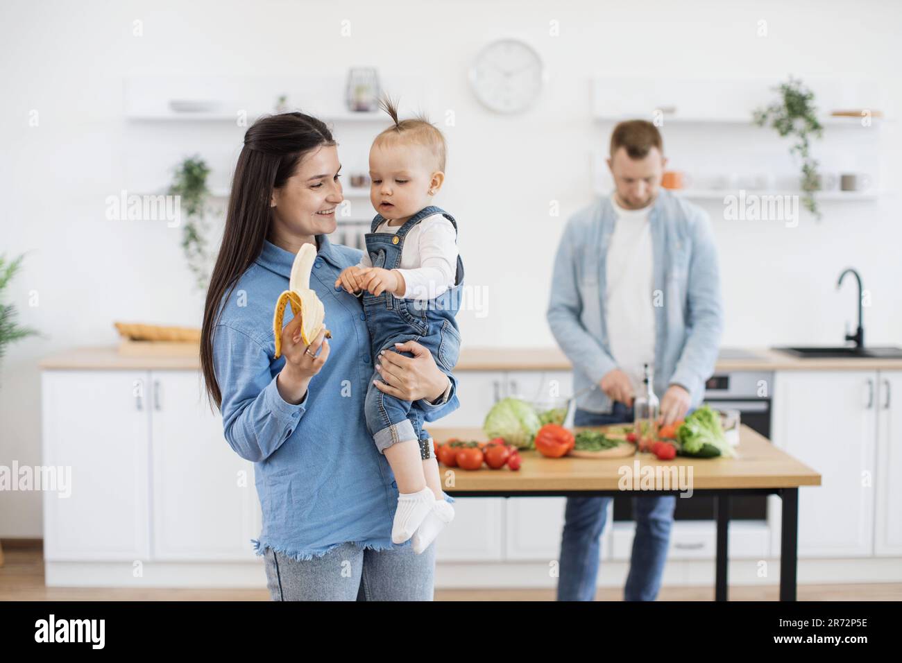 Cheerful caucasian mother proposing baby tasty banana while father ...