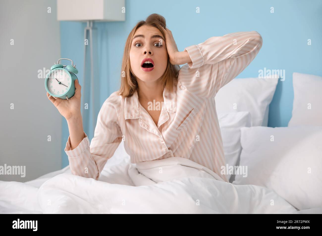 Shocked young woman with alarm clock sitting on bed in morning Stock ...