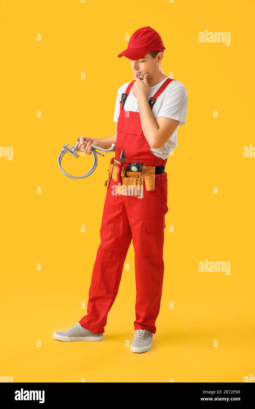 Thoughtful young plumber with flexible hose on yellow background Stock ...