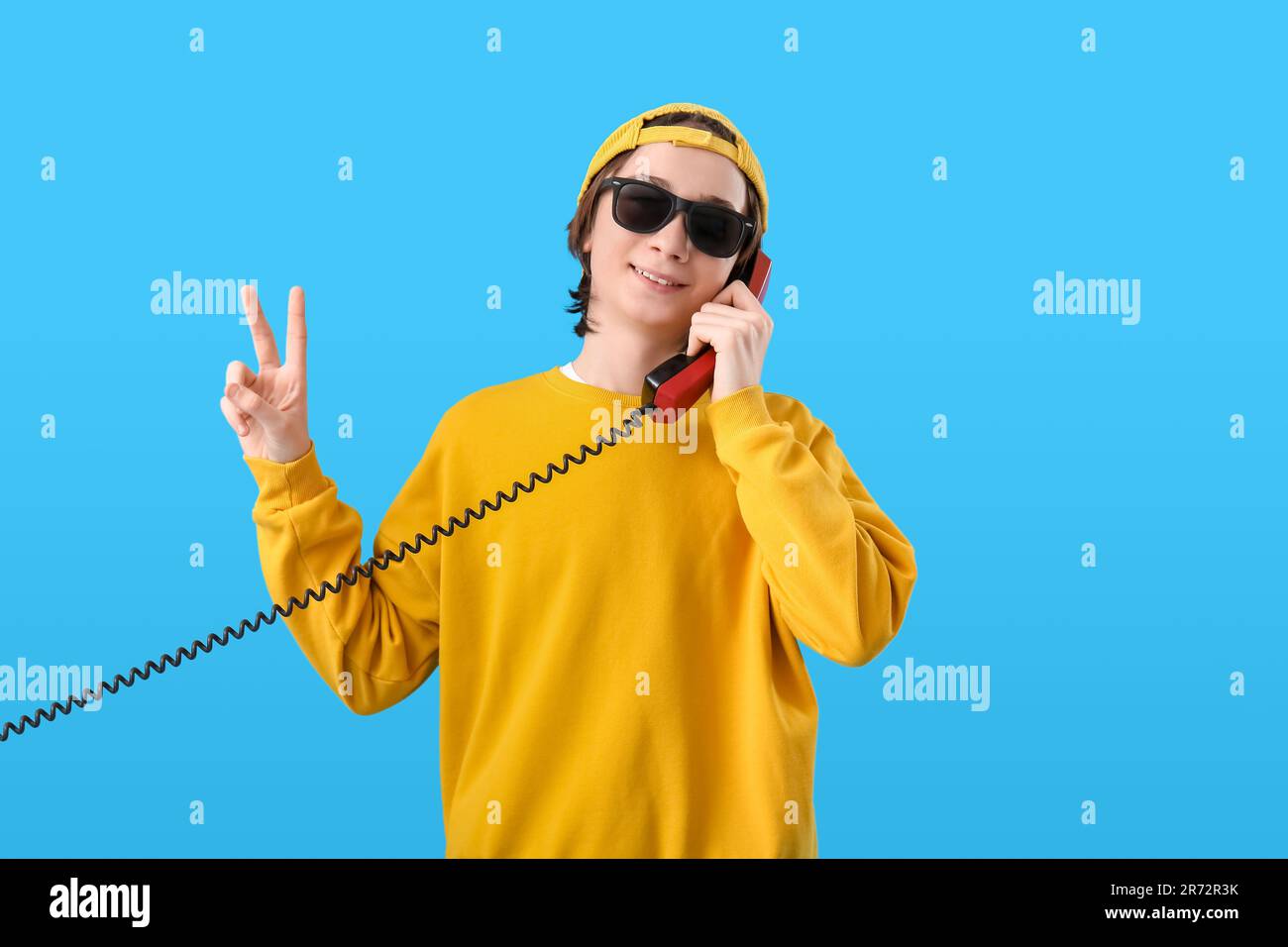 Cool teenage boy with phone receiver showing victory gesture on blue ...