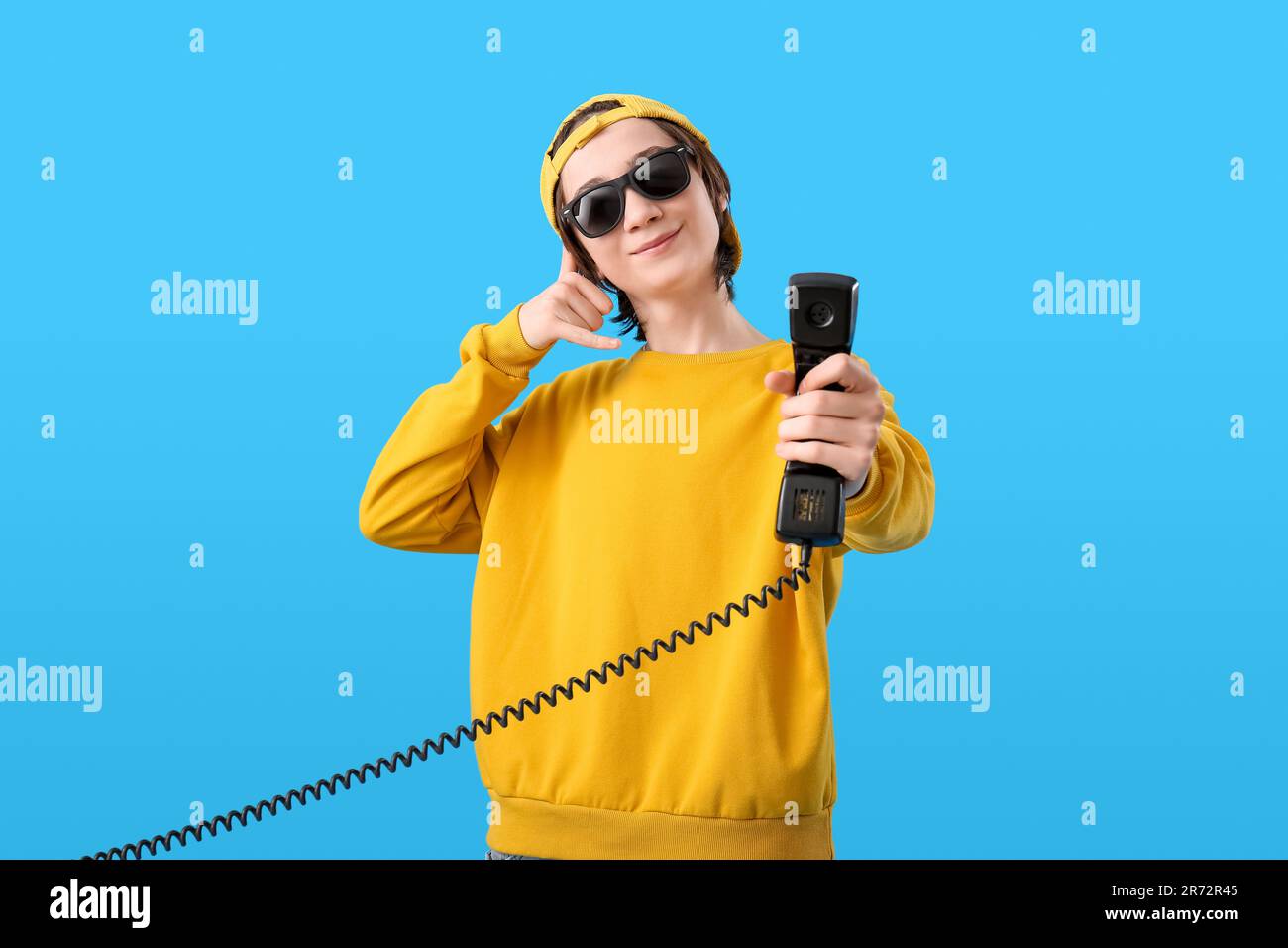 Cool teenage boy with phone receiver showing "call me" gesture on blue ...