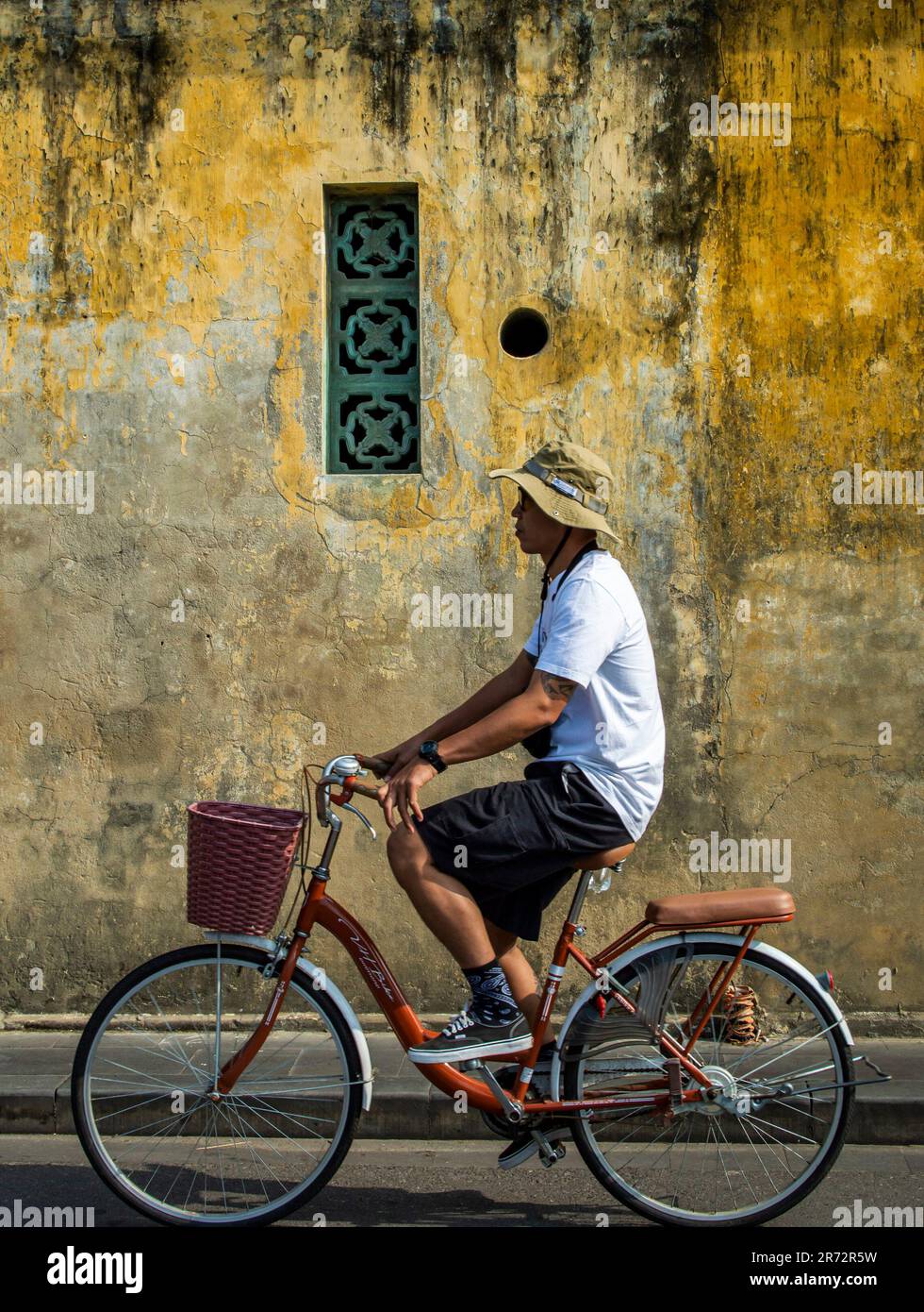 Hoian, Vietnam, March 6th, 2023. A man with hat cycling pass in front ...
