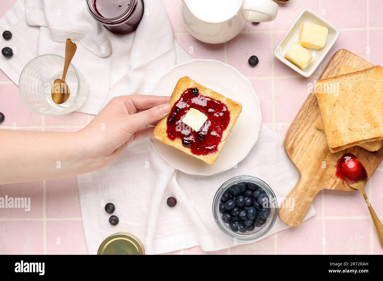 Woman holding tasty toast with blueberry jam on pink tile background ...