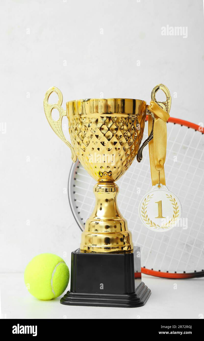 Gold cup with first place medal, tennis racket and ball on light ...
