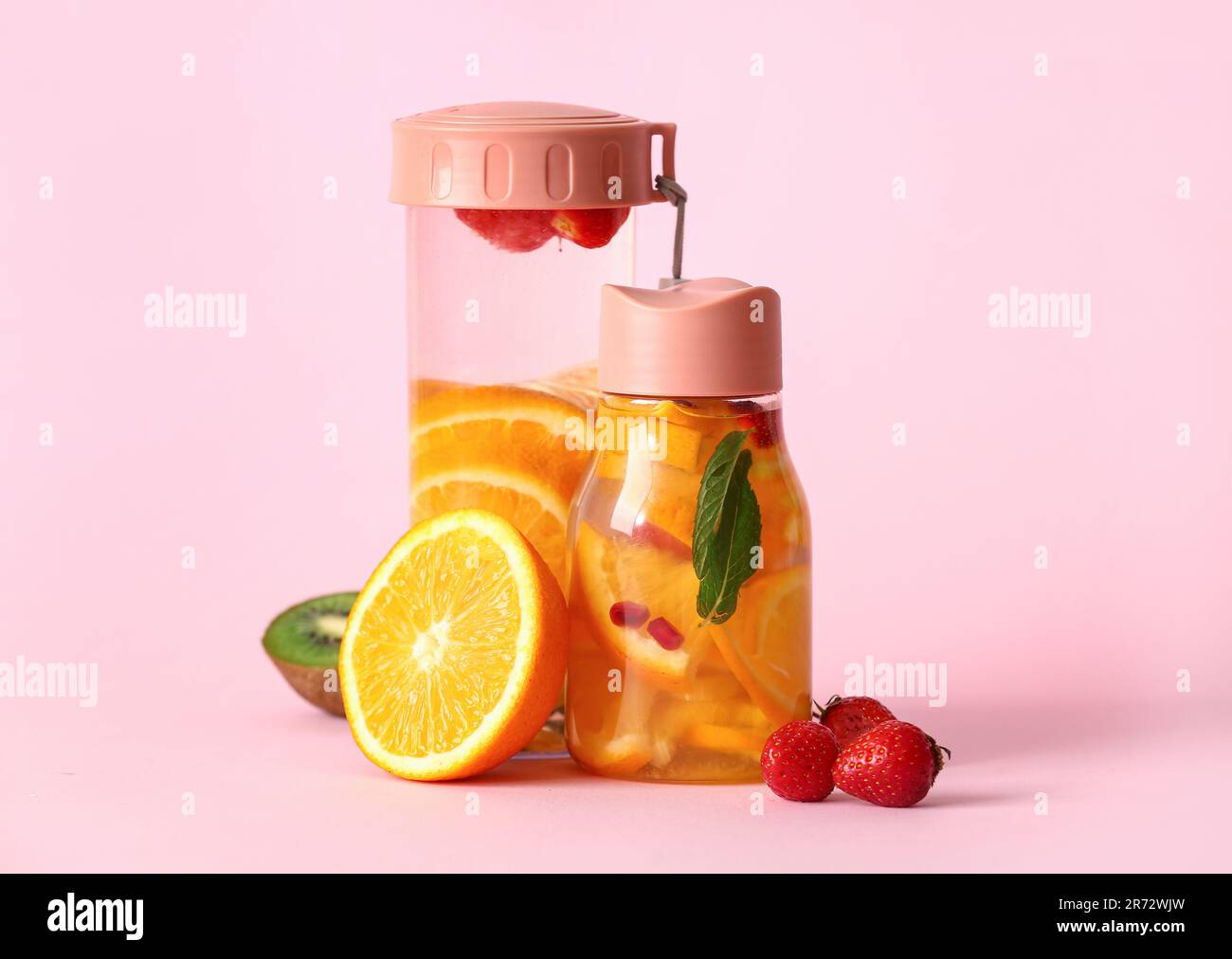 Sports bottles of infused water with different sliced fruits on pink ...