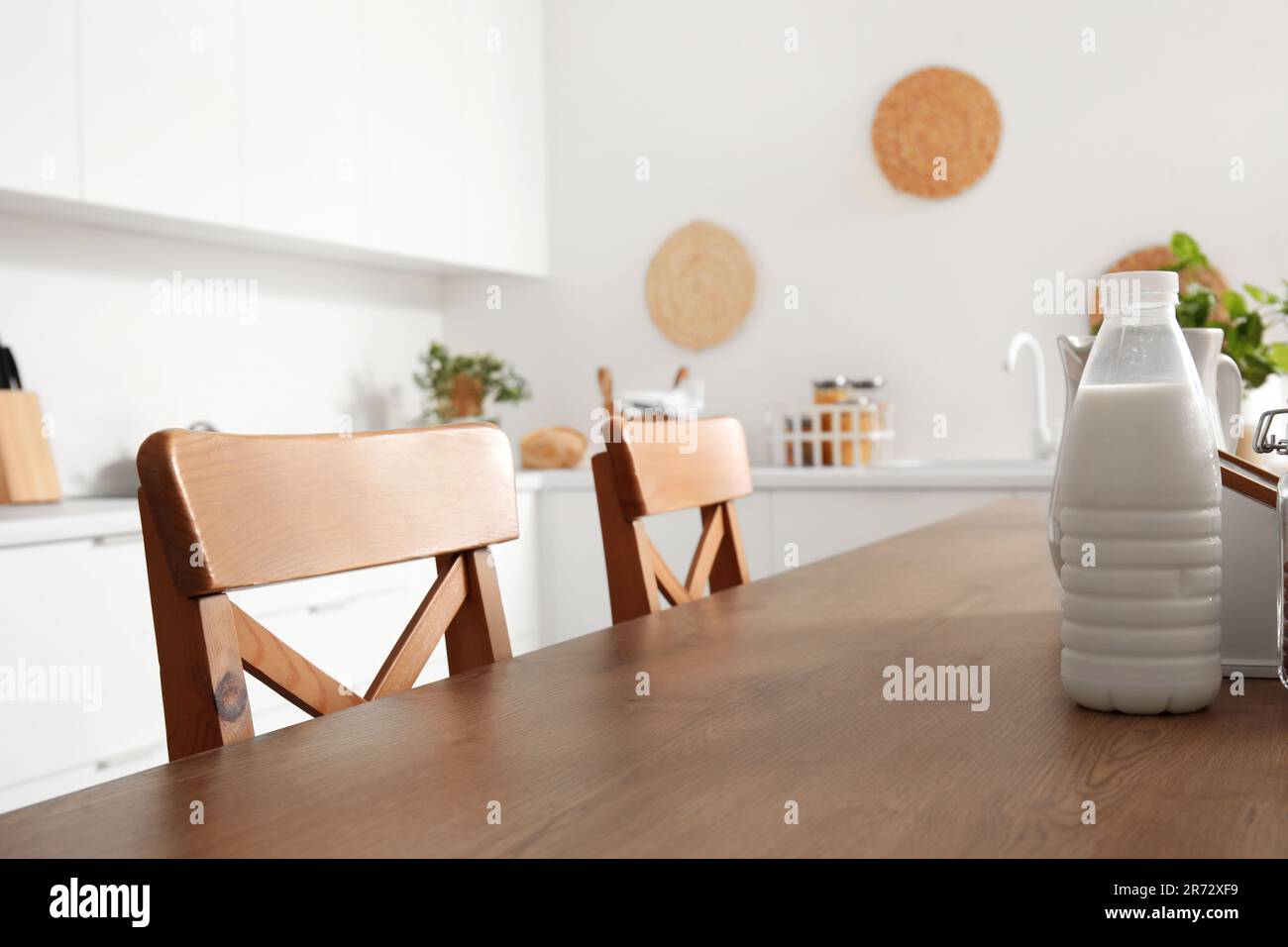 Wooden island table with bottle of milk and chairs in modern kitchen ...