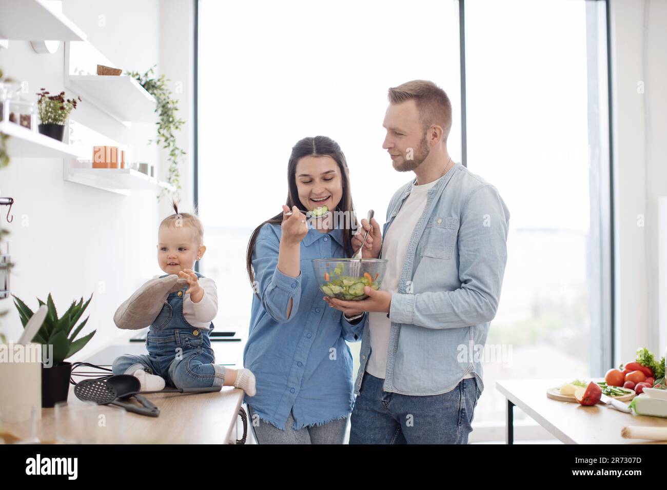 Happy mother and father eating vegetable salad while small baby sitting ...