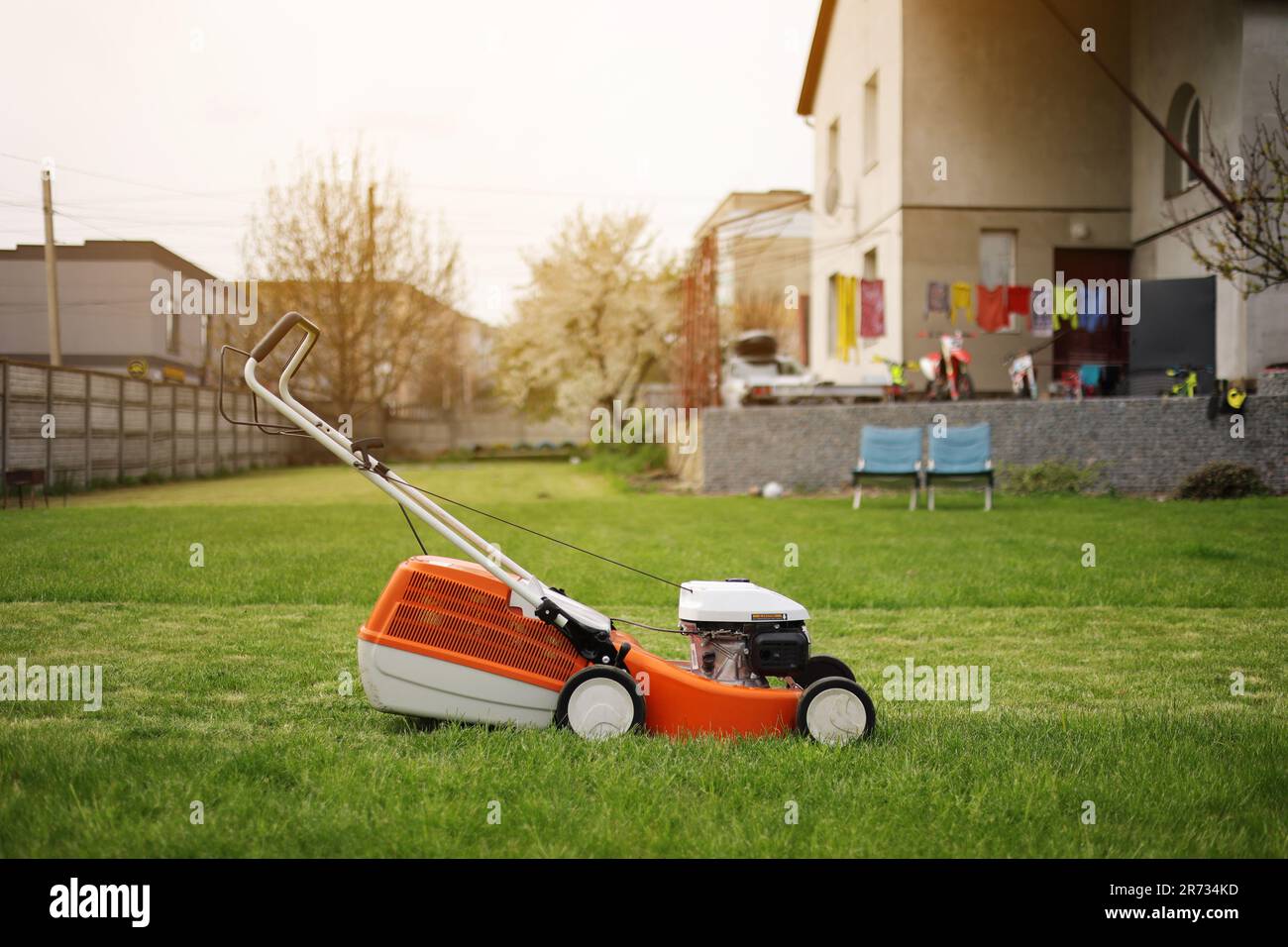 Modern orange-grey electric lawn mower on bright lush green lawn at ...