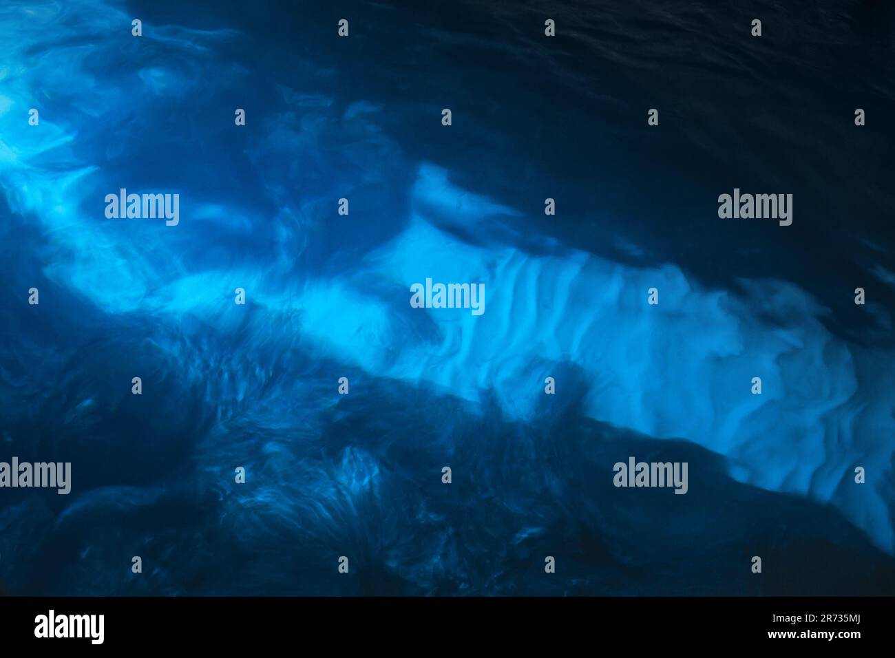 Blurred blue underwater view with white sand on a seabed and deep blue ...