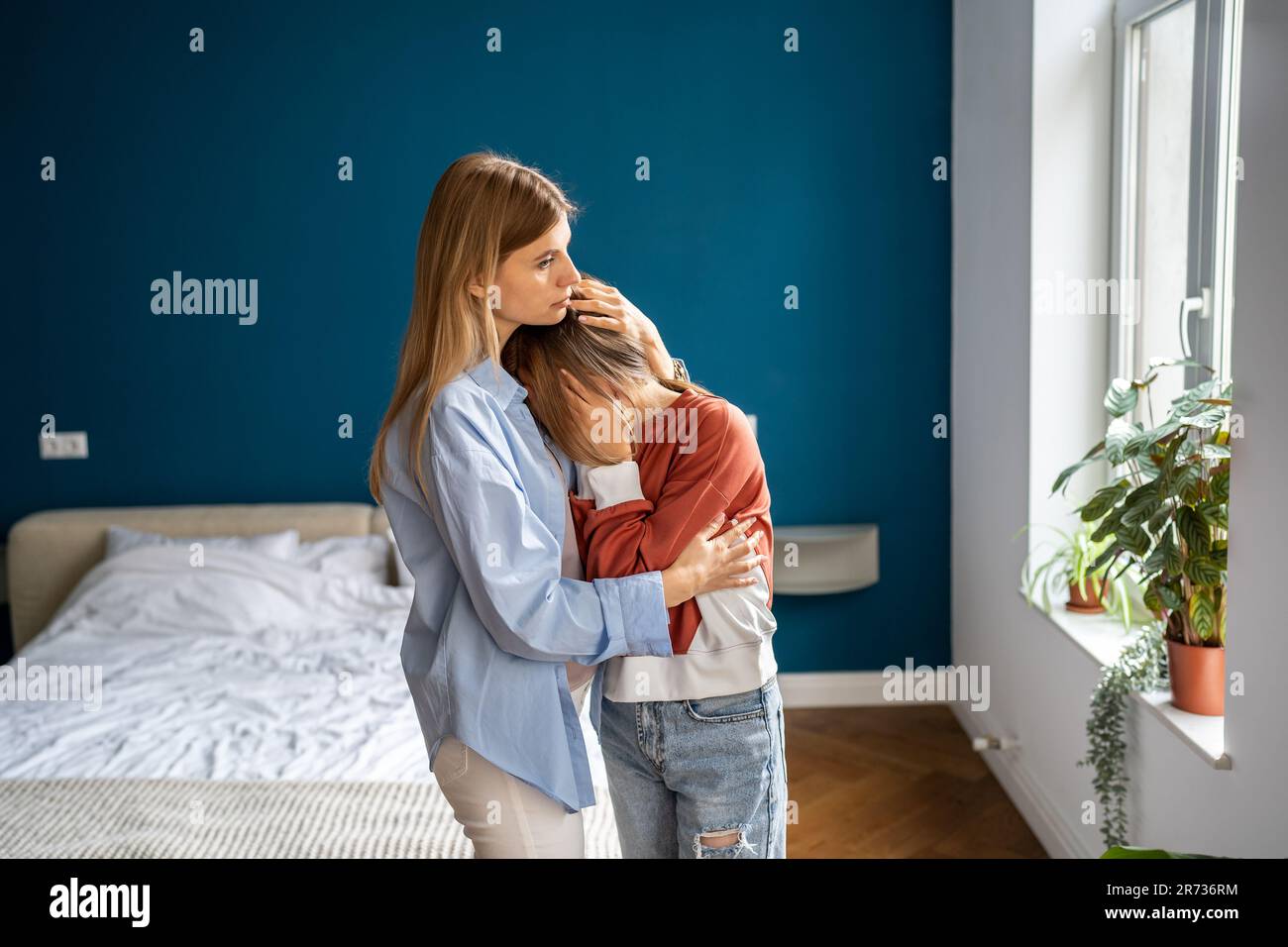 Mother hugging comforting upset crying teenage daughter at home, embracing and supporting teen ...