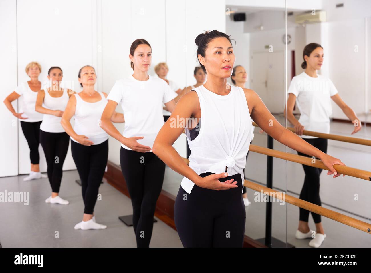 Group of women engaged in classical ballet stand holding onto a barre ...