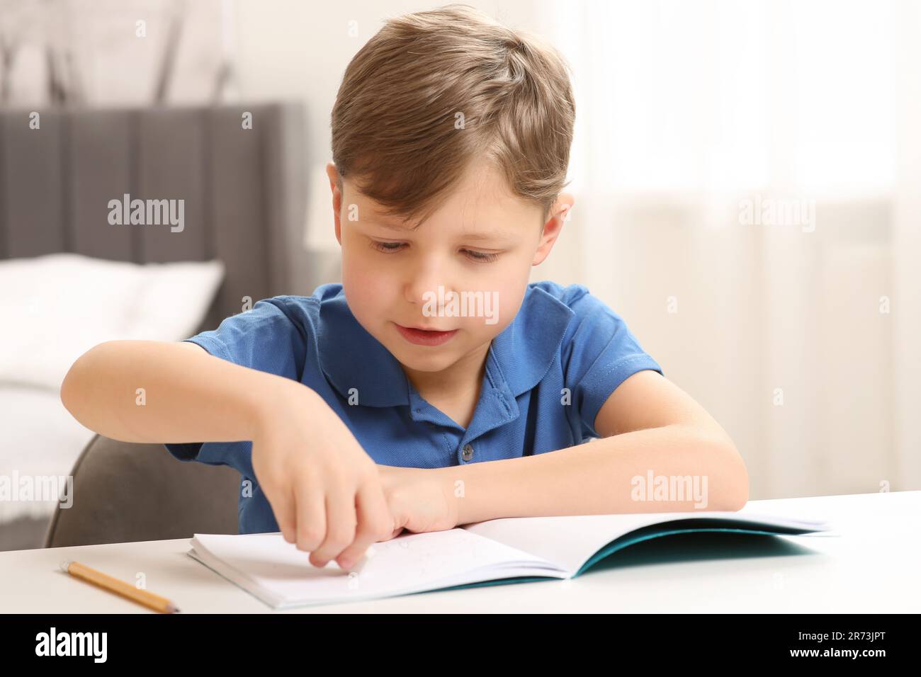 Little boy erasing mistake in his notebook at white desk indoors Stock ...