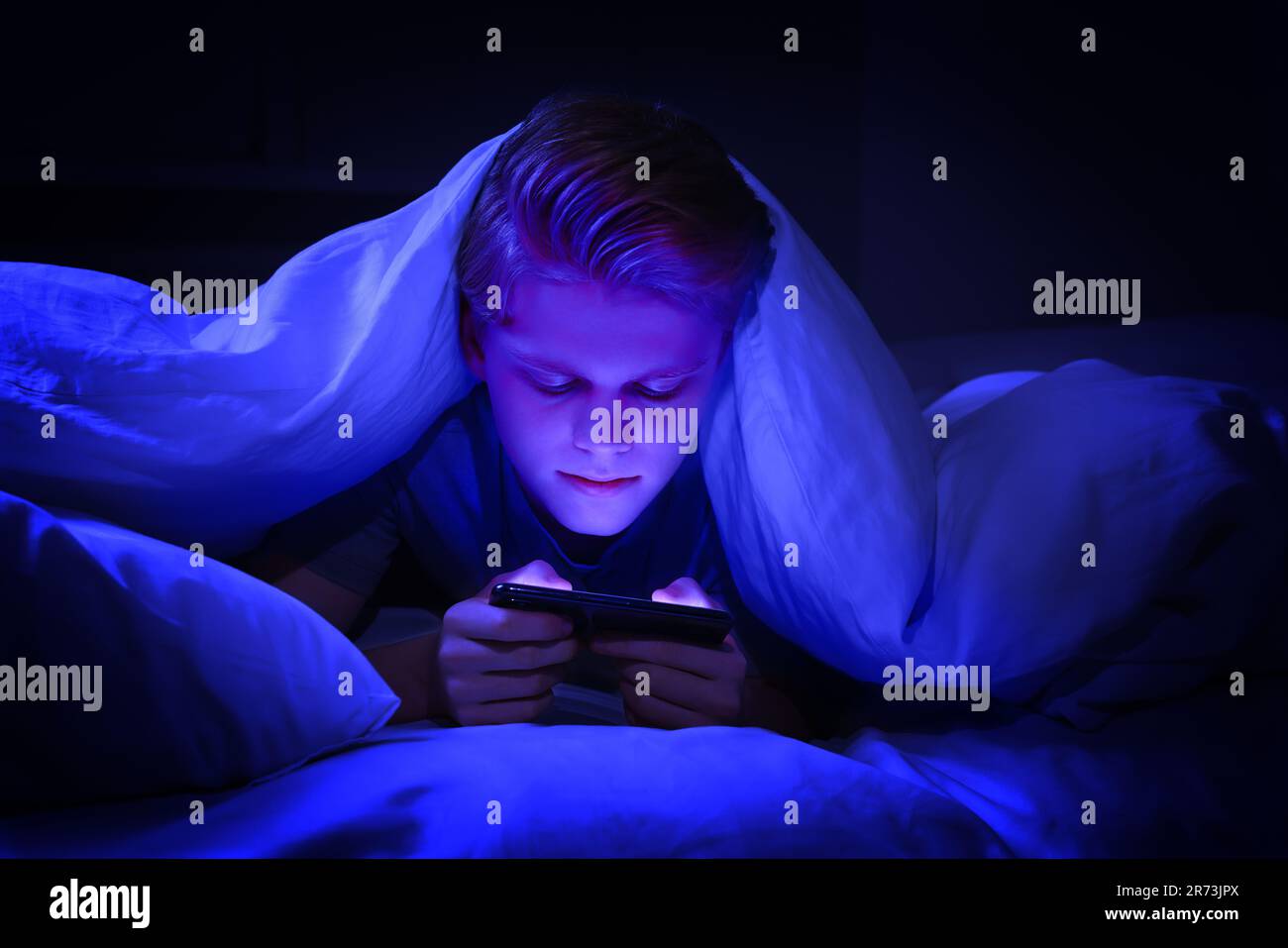 Internet addiction. Teenage boy using smartphone under blanket on bed ...