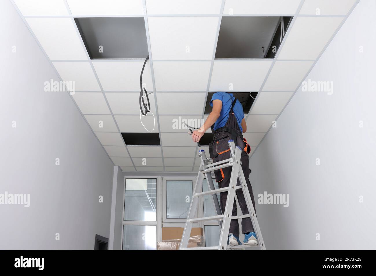 Installing ceiling lighting. Electrician working on step ladder in room ...