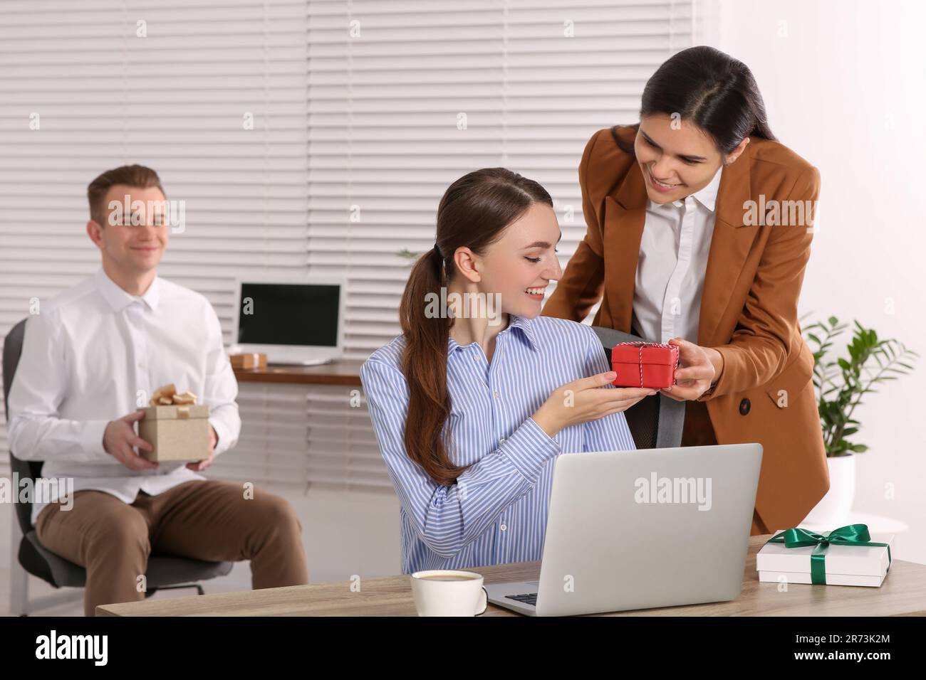 Woman presenting gift to her colleague in office Stock Photo - Alamy