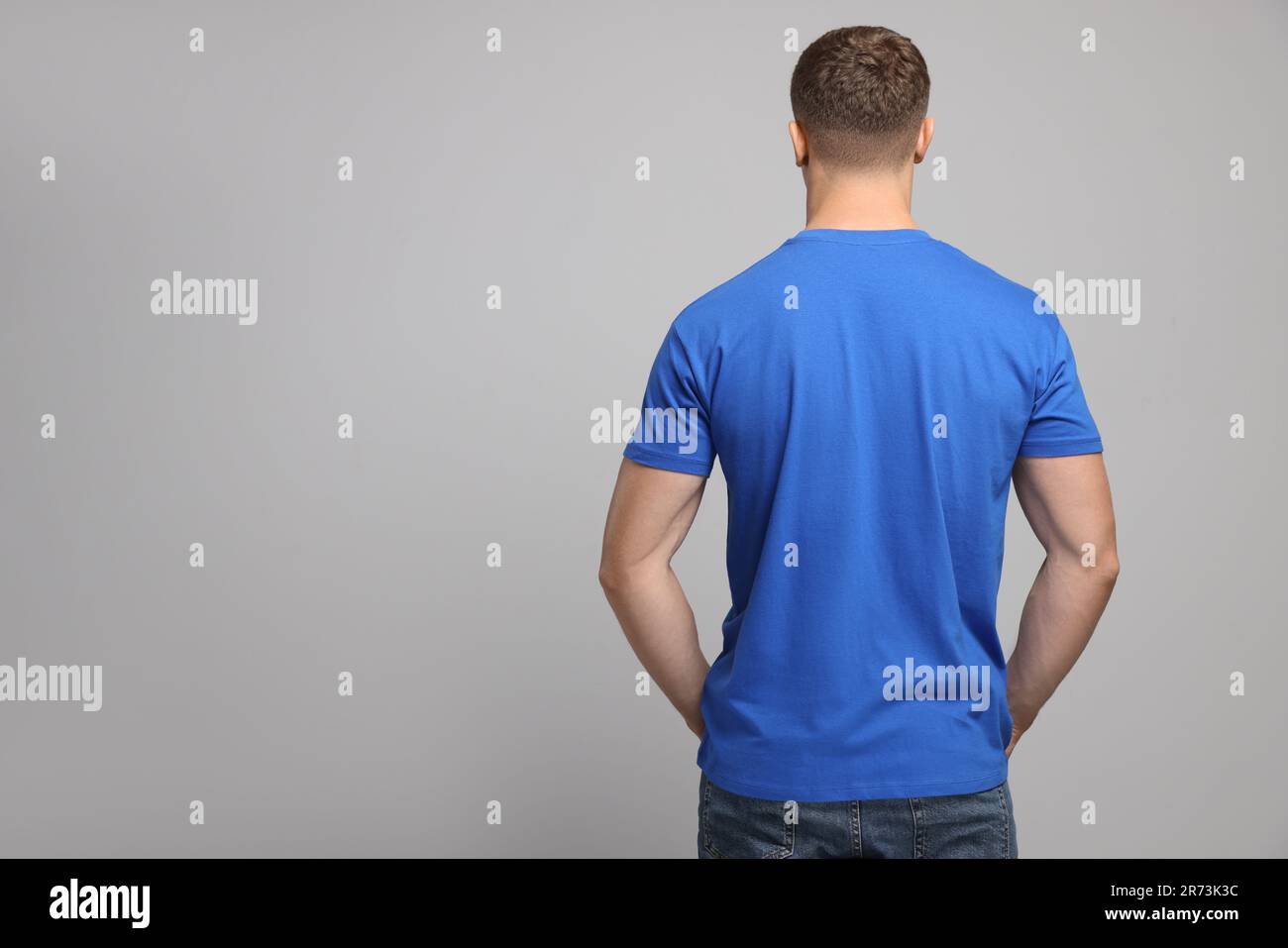 Man wearing blue t-shirt on light grey background, back view. Mockup ...