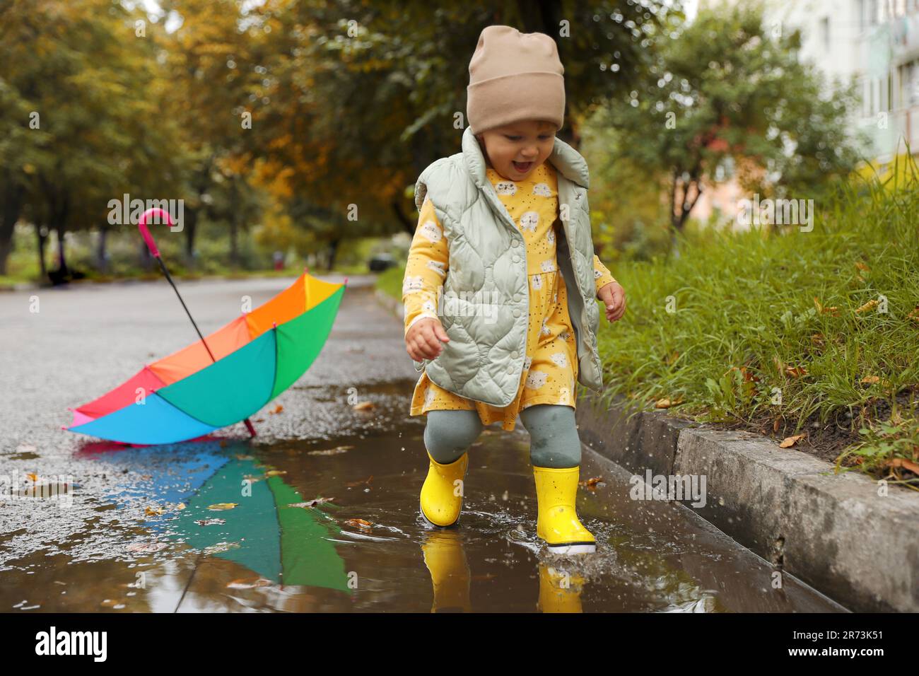 Cute little girl splashing water with her boots in puddle outdoors ...