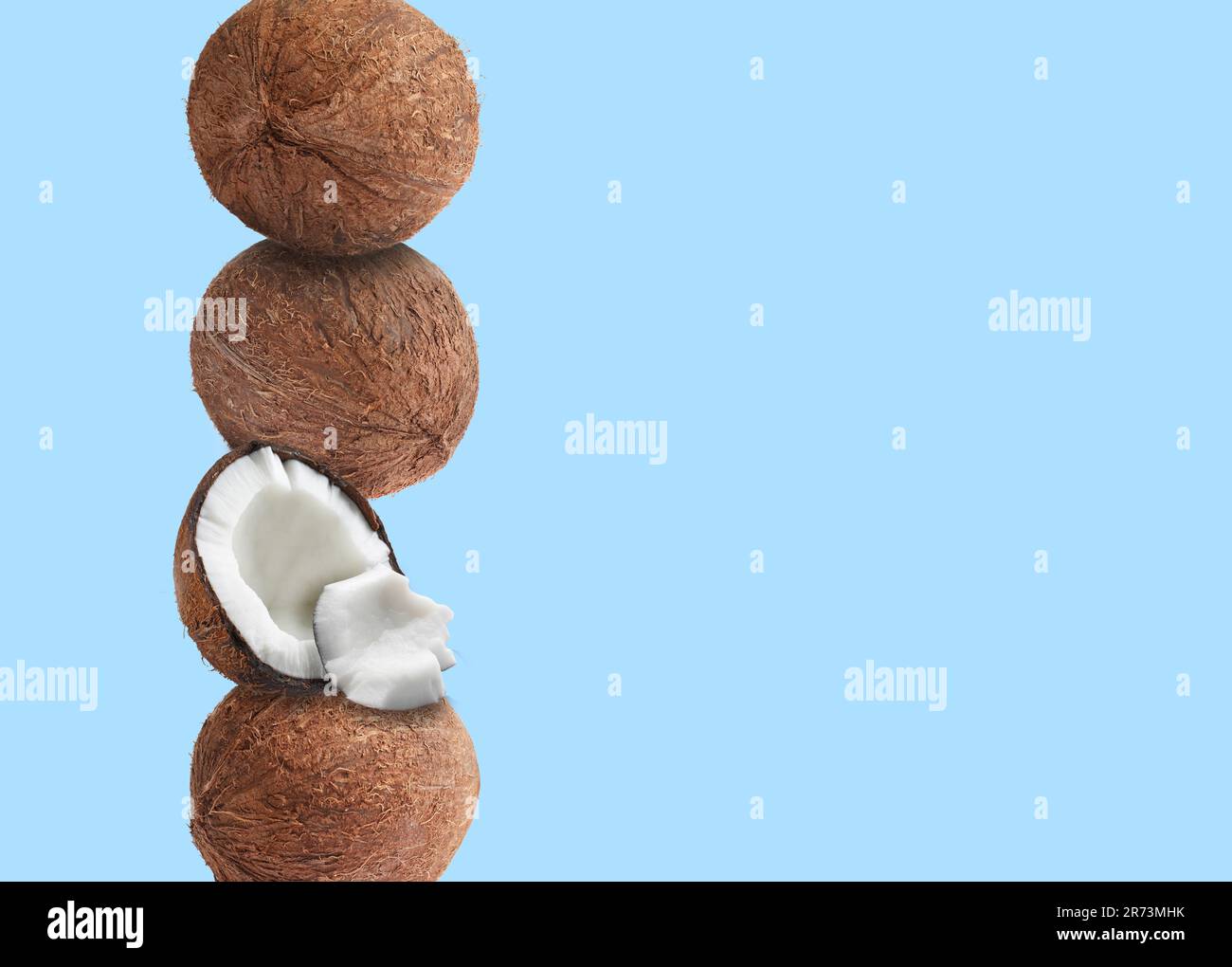 Stack of fresh coconuts on pale light blue background. Space for text ...