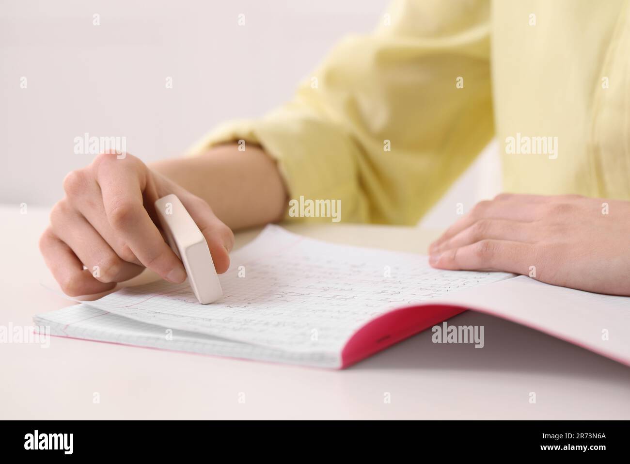 Girl erasing mistake in her notebook at white desk indoors, closeup ...