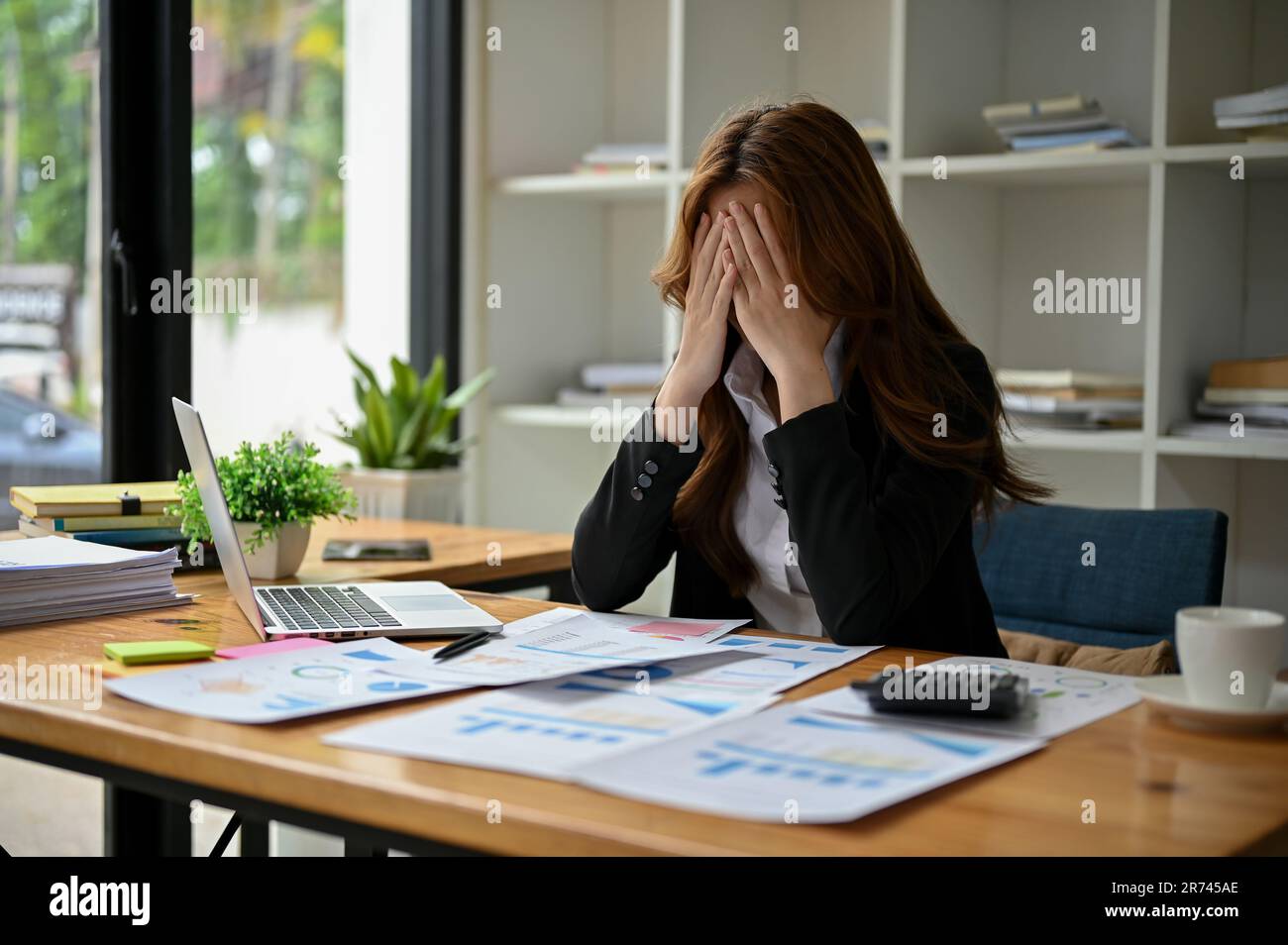 A frustrated and upset young Asian businesswoman covering her face with ...