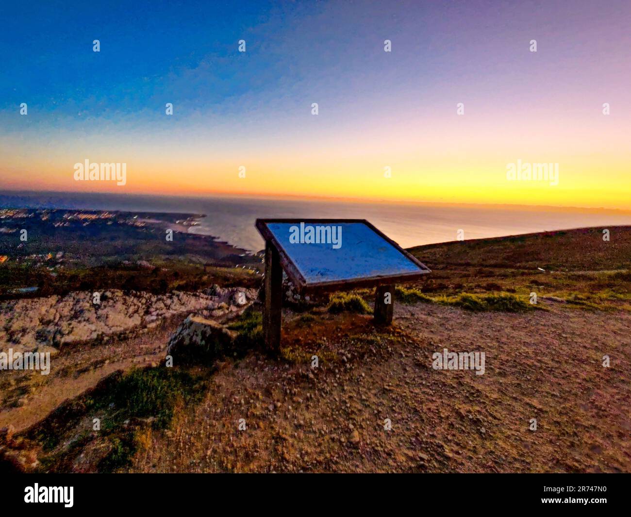 An isolated wooden board on a grassy hilltop overlooking a sun-kissed ...