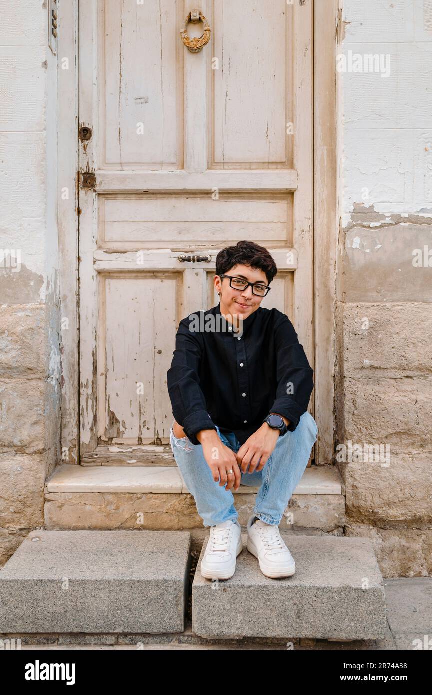 Young transgender man posing sitting on the front steps of a house ...