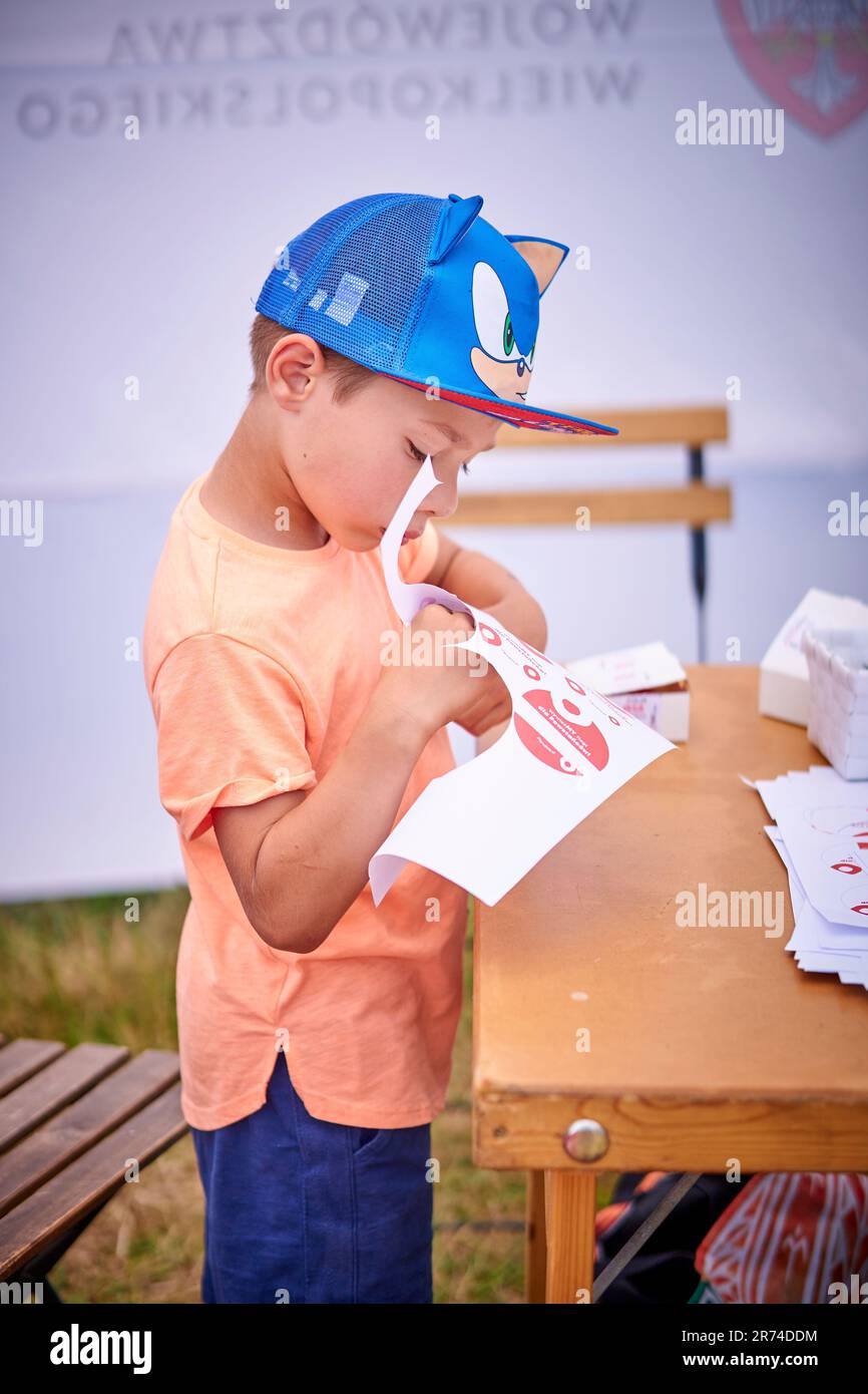 A cheerful young boy playing with stickers in a park under a white tent ...
