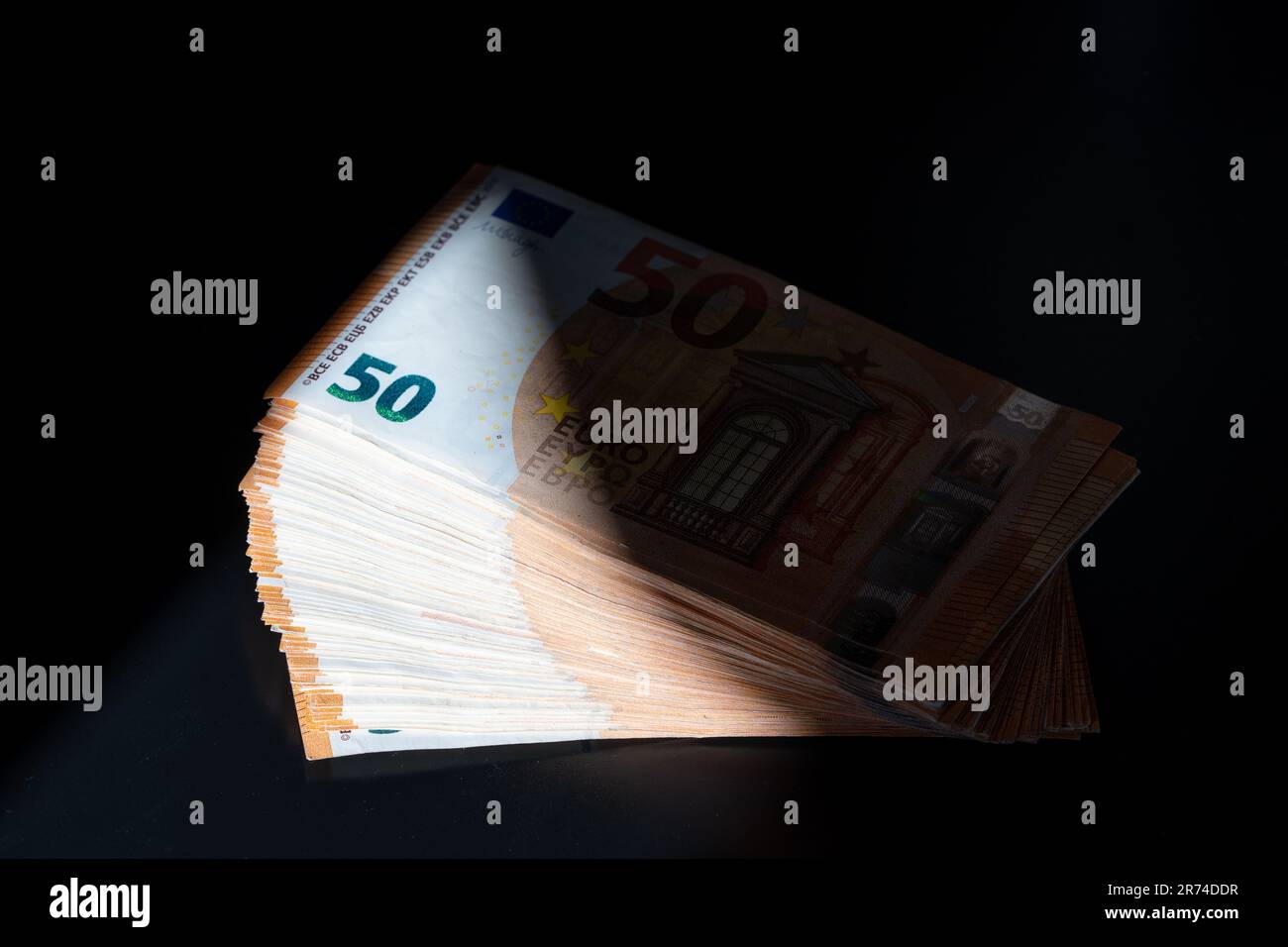 A big wad of money half in the shade on the black table. Euro money ...