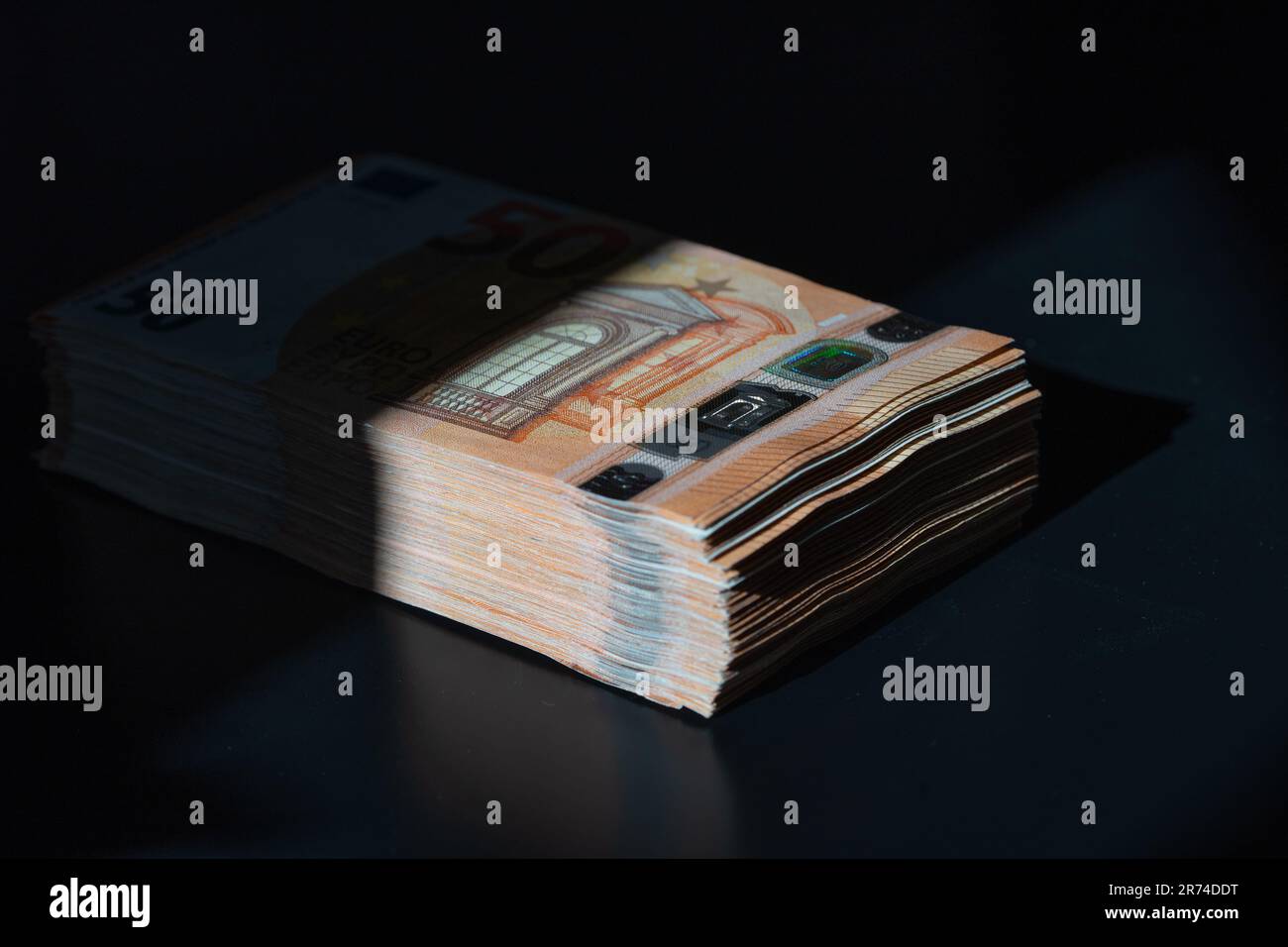 A big wad of money half in the shade on the black table. Euro money ...