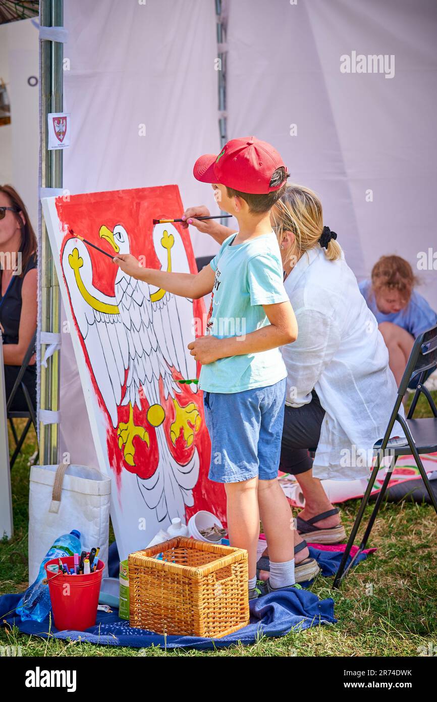 A young boy artist painting the Polish coat of arms on canvas in a lush ...