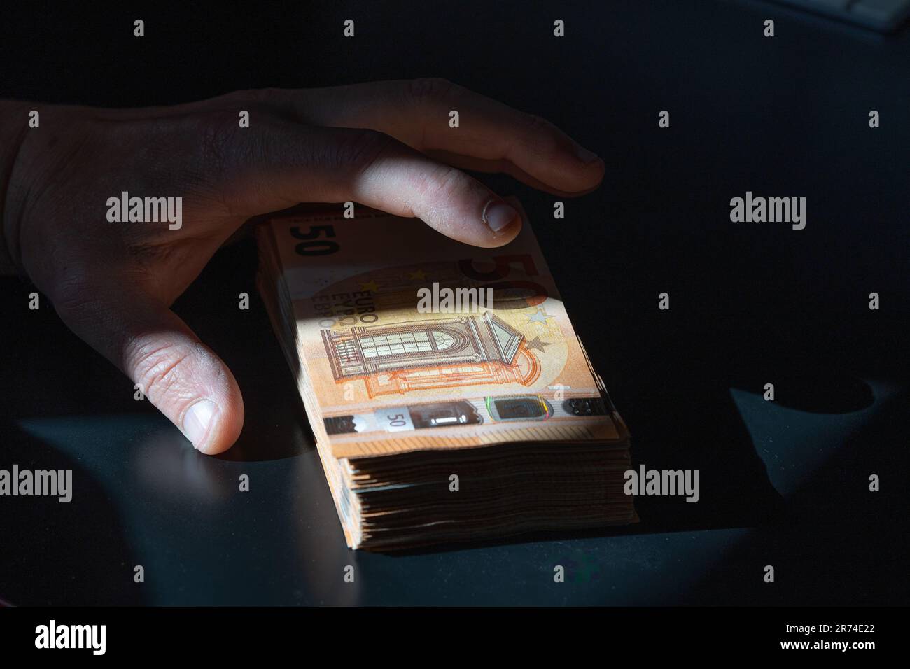 A human hand reaches for a wad of money half in the shade. Euro money ...