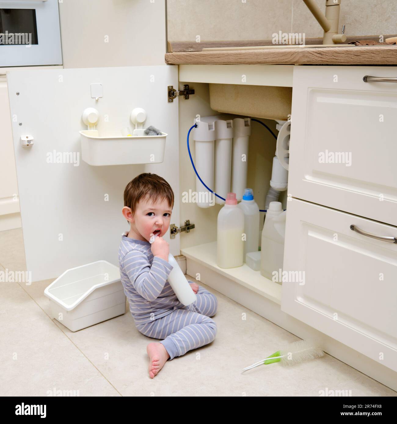 A child is playing with chemical cleaning products under the sink in ...