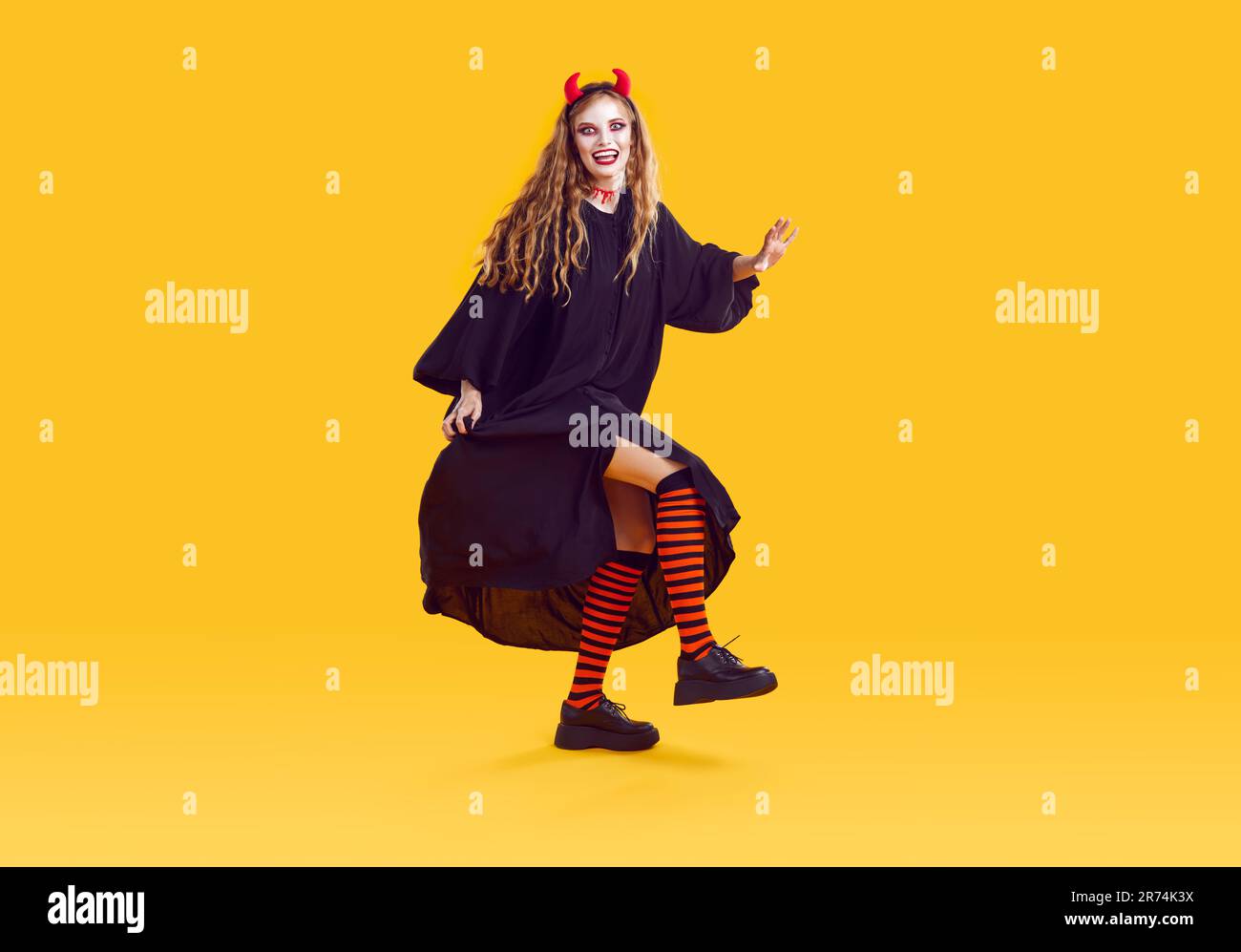 Cheerful young woman in devil costume has fun dancing at Halloween ...