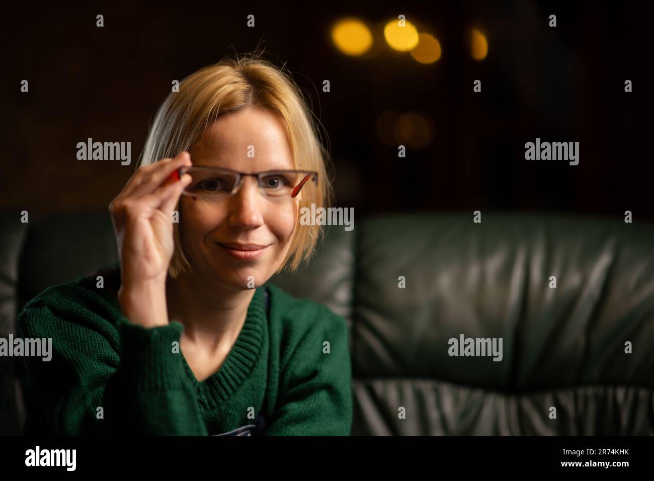 A woman with glasses in her hands looks at the camera in a dark room ...