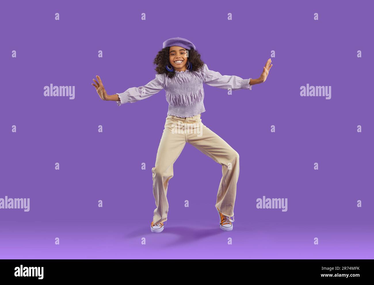 Happy cheerful child in trendy causal outfit dancing on purple studio ...