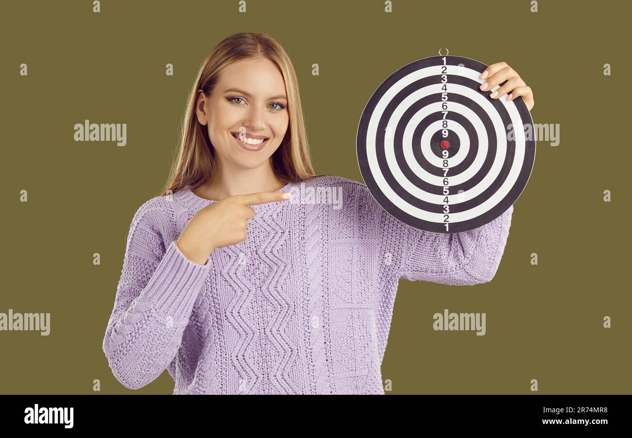 Smiling blondy woman holding dartboard shooting target and pointing ...