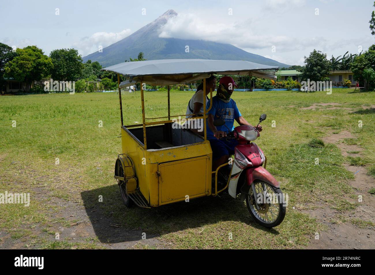 Mayon Volcano is seen as a tricycle passes by an evacuation center in ...