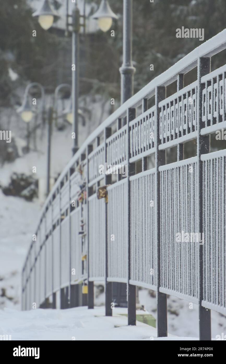 A snow-covered footpath extends along a metal railing, in a winter ...