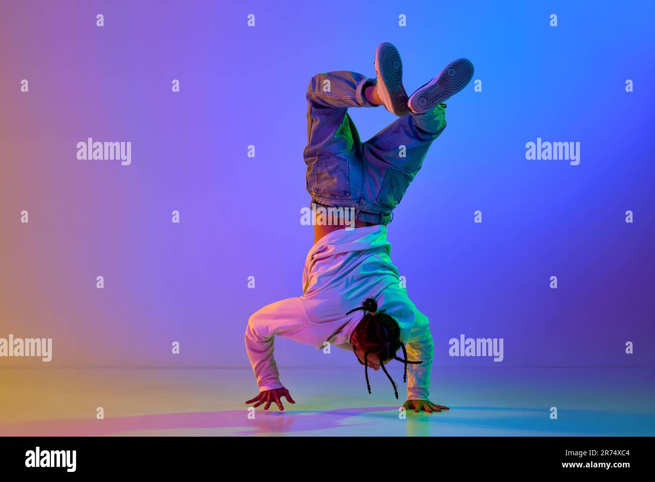 Flexible young man, contemp dancer performing breakdance, hip-hop against gradient multicolored ...