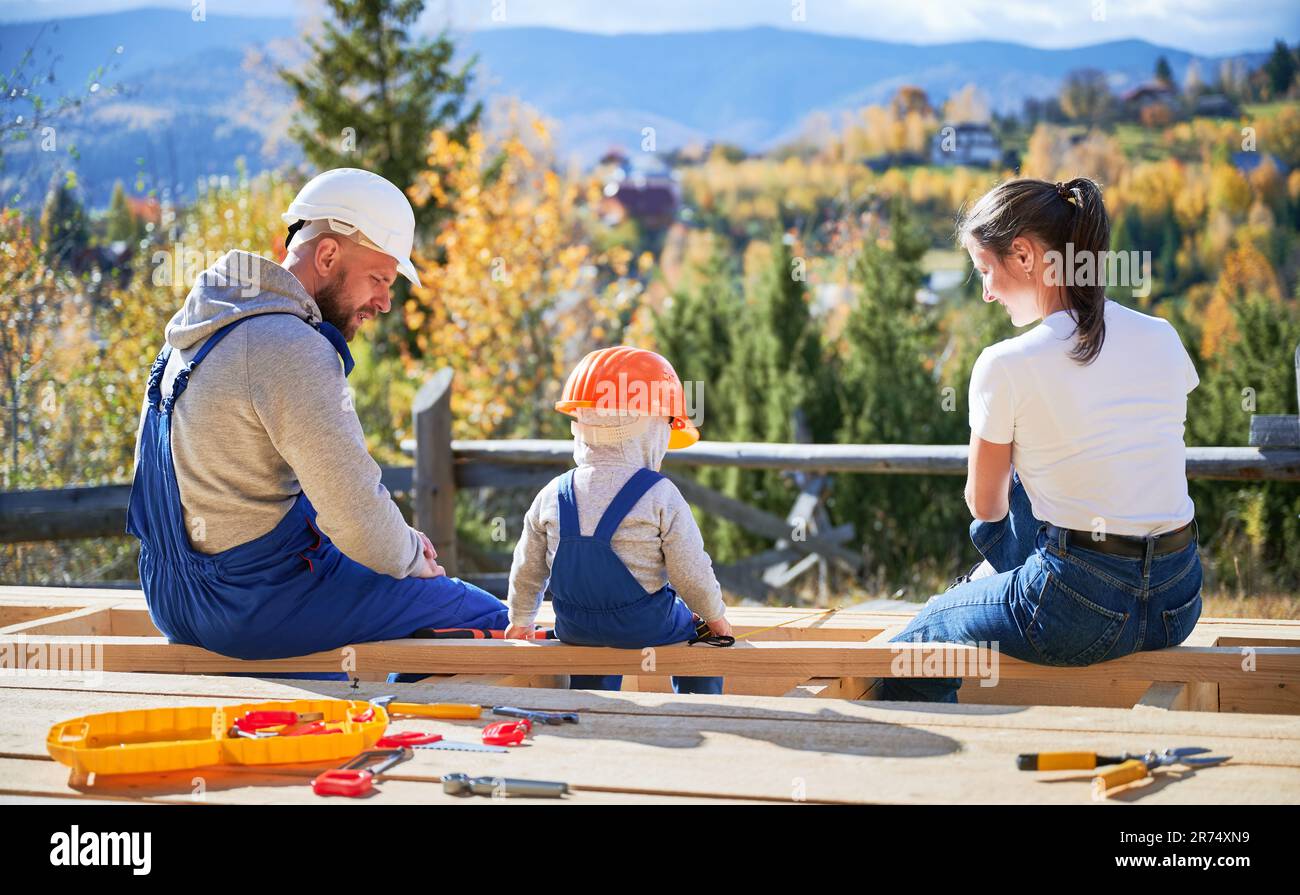 Back view of father, mother and son building wooden frame house ...