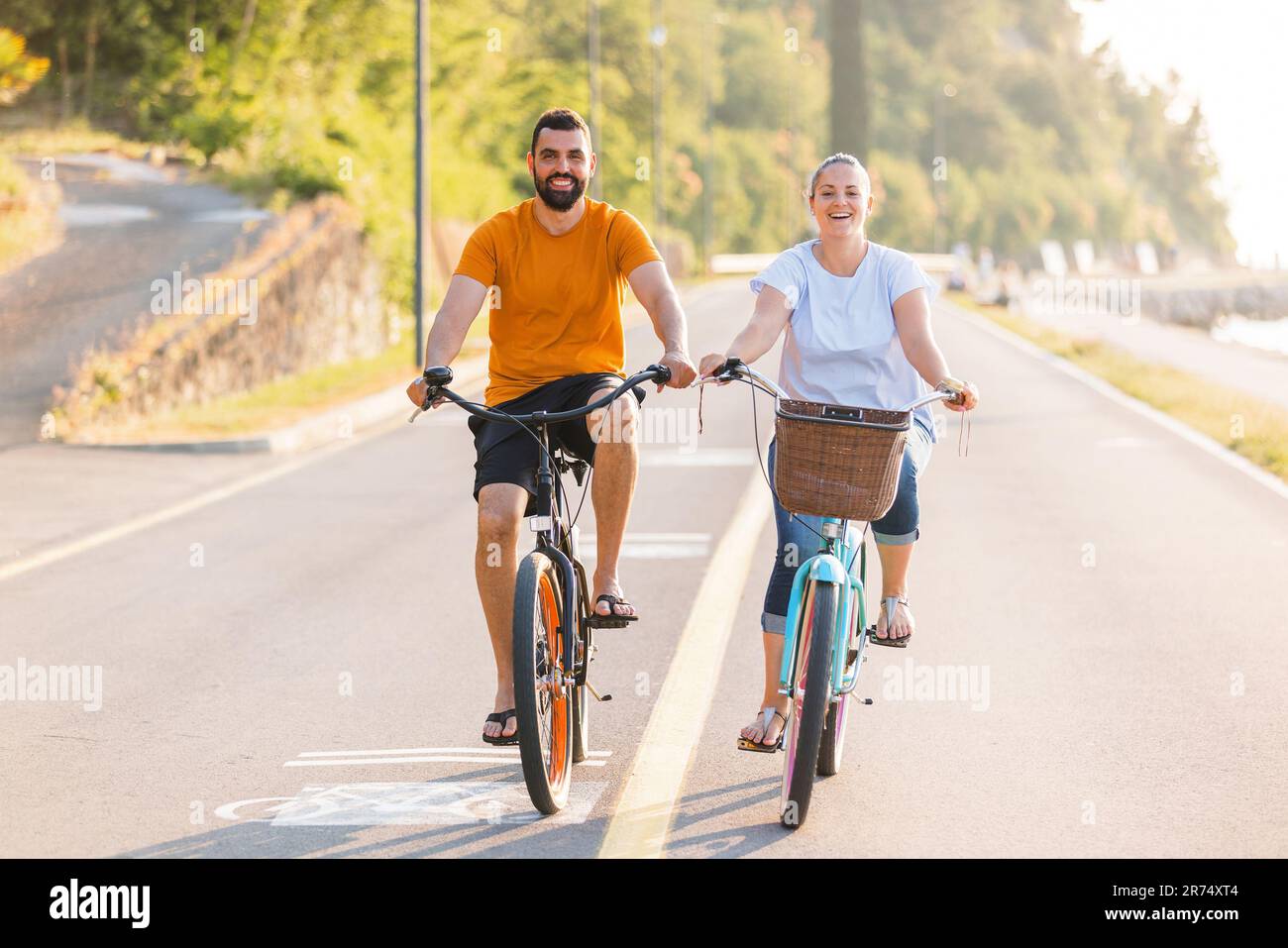 Couple taking pleasure in the ride on beach cruiser bikes, pedaling on ...
