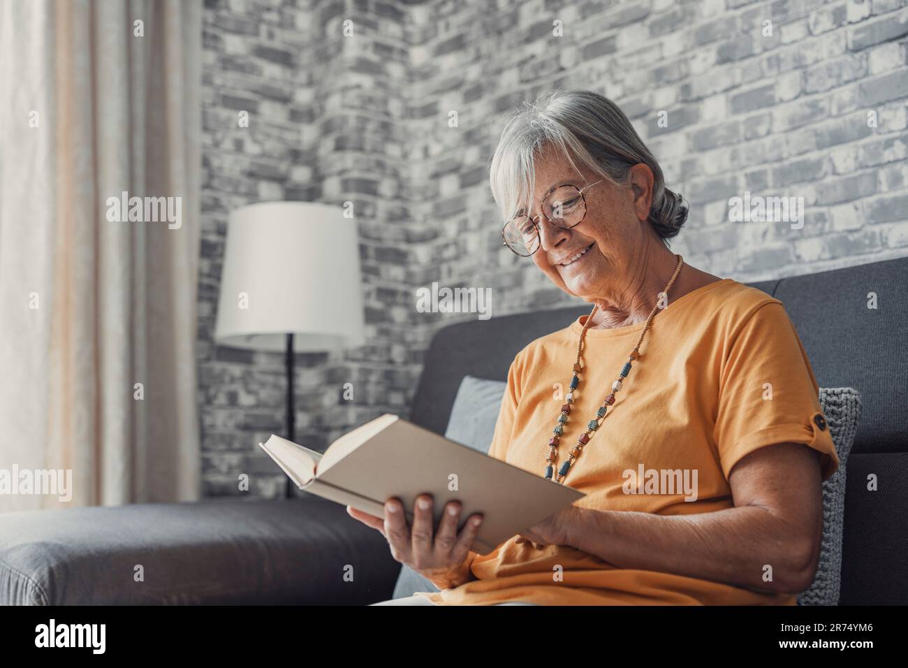 Happy older blonde woman sitting on comfortable sofa in living room ...