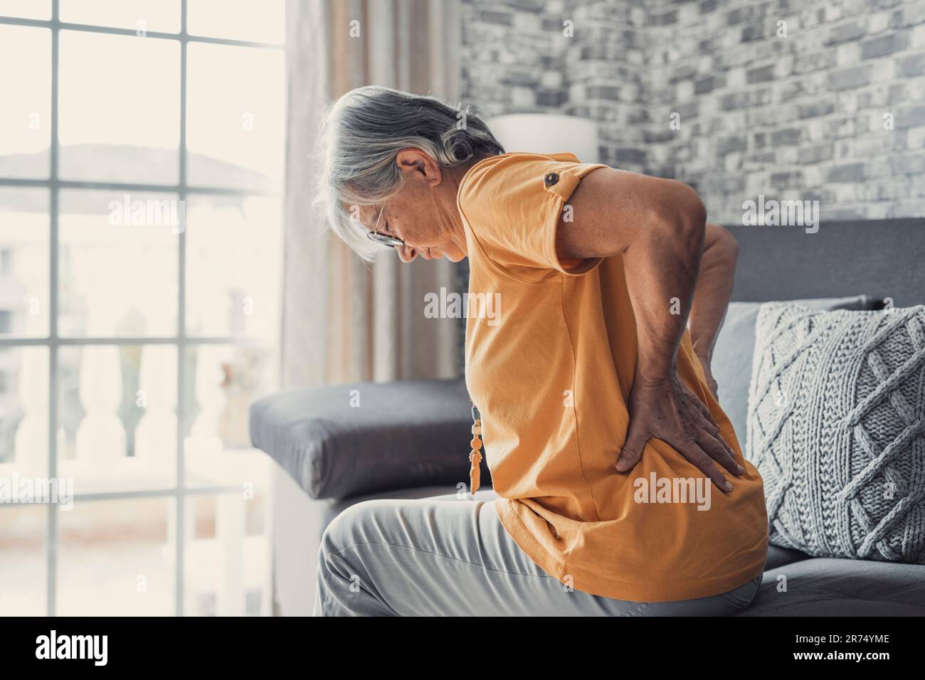 Unhappy mature woman touching back, feeling pain, sitting on couch in ...