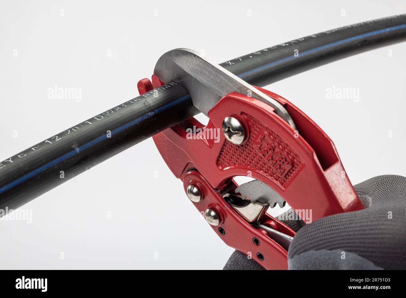 Hand with work glove cuts plastic pipe with plastic pipe cutter, white ...