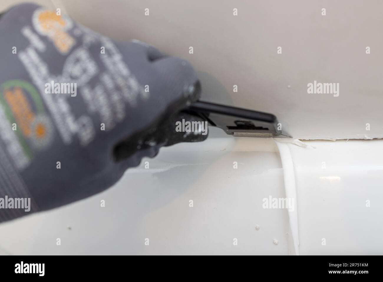 Workmen remove old silicone joints on bathtub with joint knife, detail ...