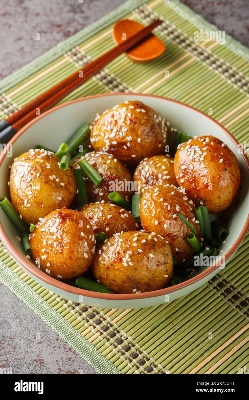 Glazed potatoes served with green onions and sesame seeds close-up in a ...