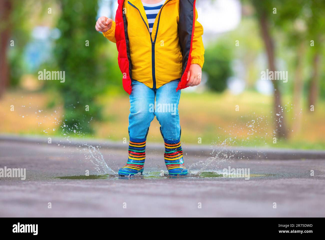 Happy toddler boy with umbrella and color rubber boots jump on a rainy ...